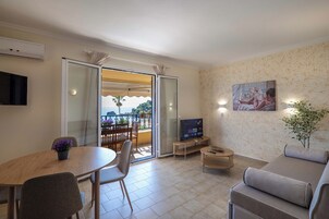 Uma sala de estar com sofá, televisão, mesa de jantar com cadeiras e varanda com vista.