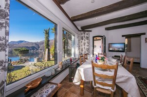 Uma sala de jantar com mesa posta para dois, televisão e vista para um lago e montanhas.