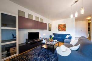 Uma sala de estar moderna com televisão de tela plana, uma mesa de centro, um sofá azul e um tapete estampado.