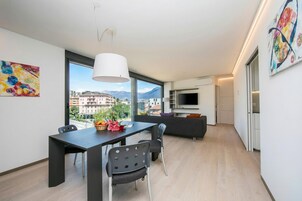 Uma sala de estar moderna com área de jantar, janelas amplas e vista para edifícios e montanhas.