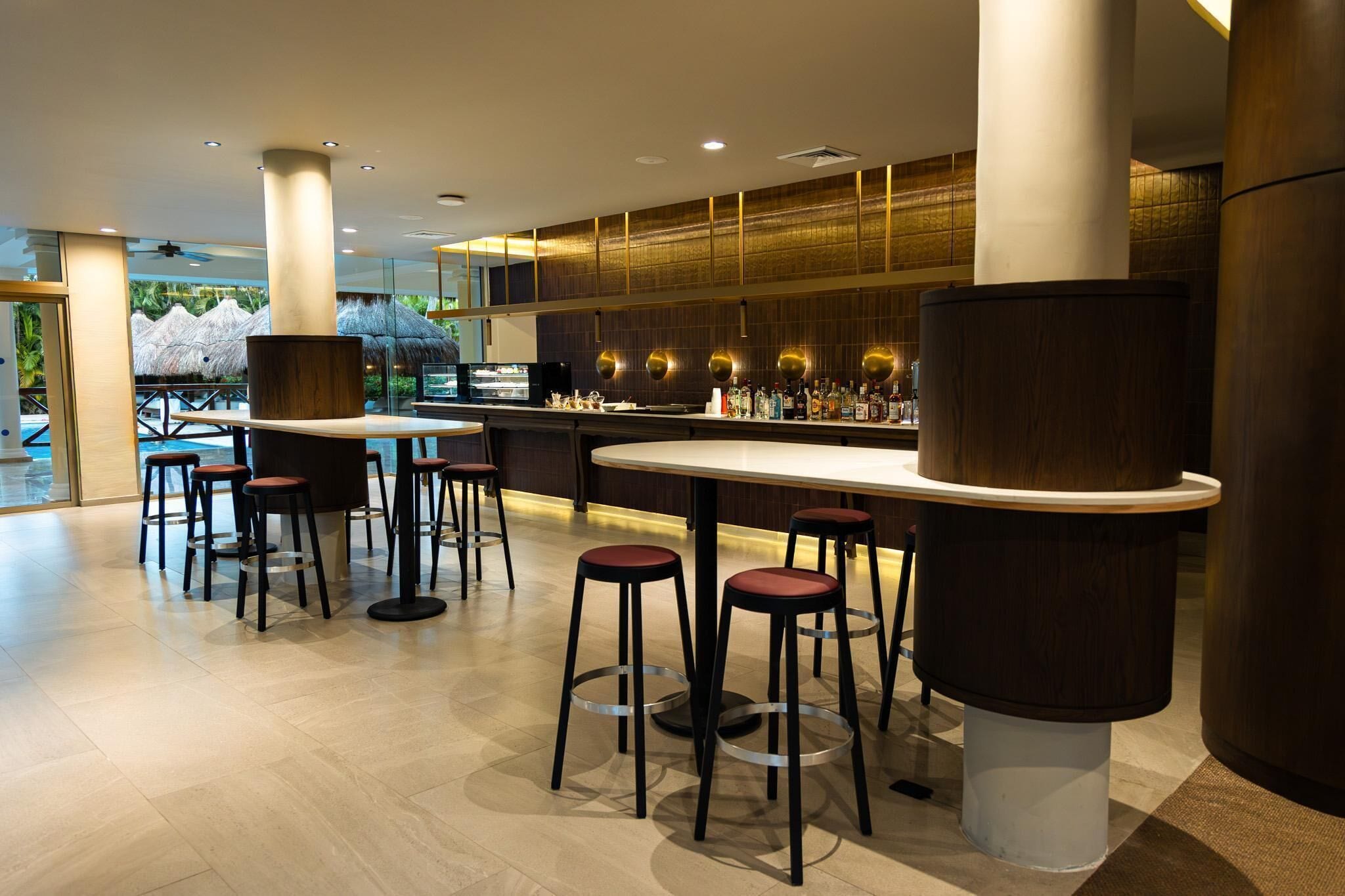 Uma área de bar moderna com banquetas altas, balcão e vista para uma área de piscina.