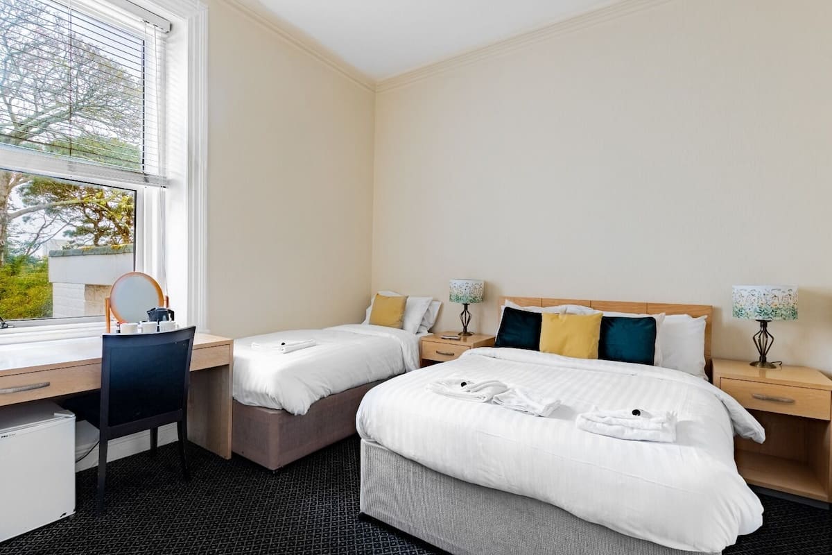 Quarto de hotel com duas camas, uma mesa e uma cadeira.