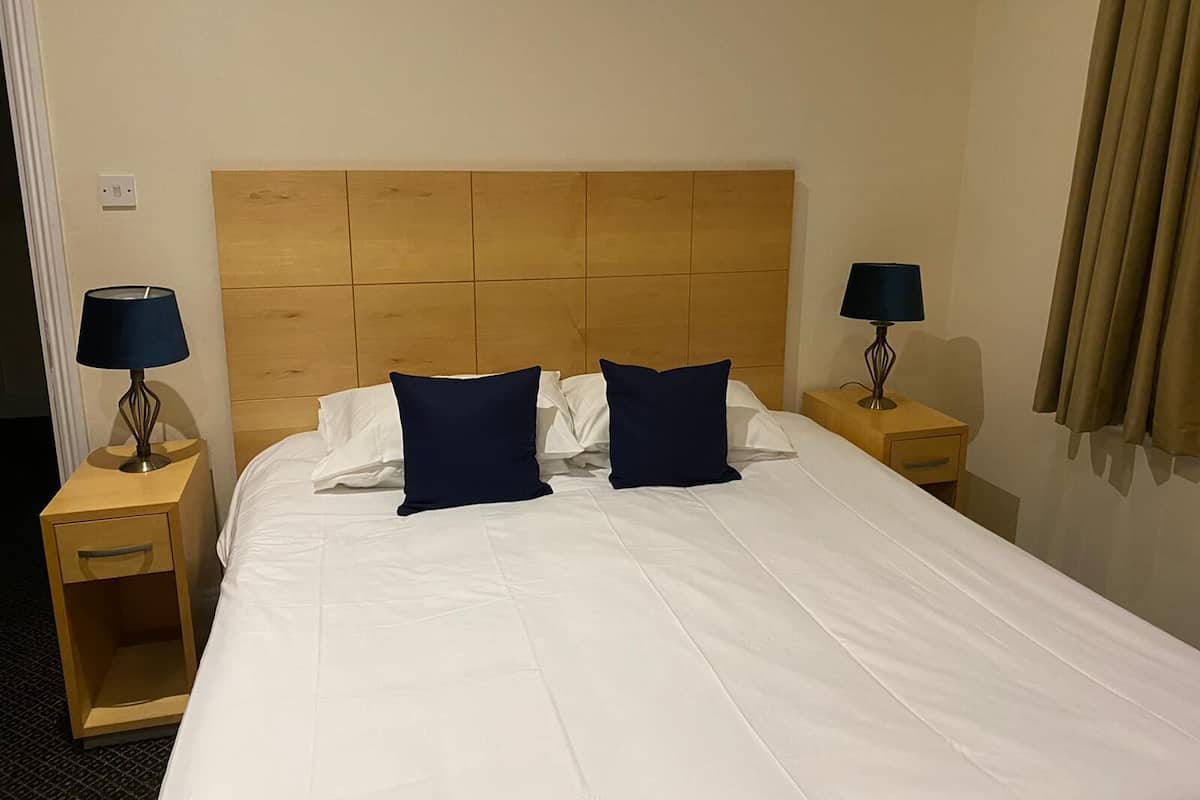 Quarto de hotel com uma cama grande, duas mesas de cabeceira e duas luminárias.