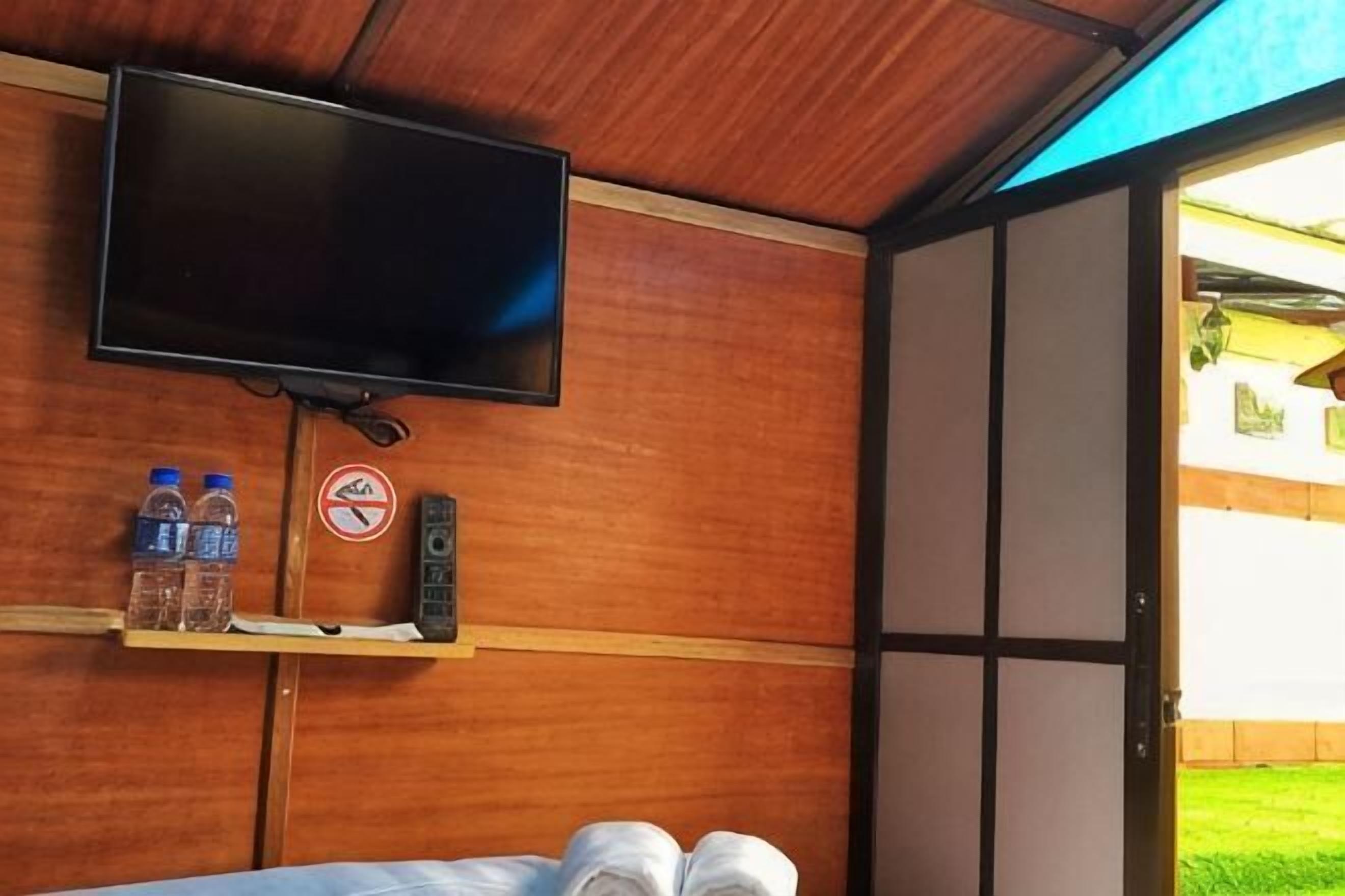 Quarto com televisão, garrafas de água, controle remoto e porta que dá para uma área externa.