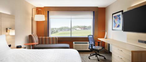 Quarto de hotel com cama, escrivaninha, cadeira, sofá, televisão e janela com vista para o exterior.