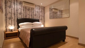 Quarto com cabeceira preta, mesa de cabeceira com abajur e um espelho grande na parede.