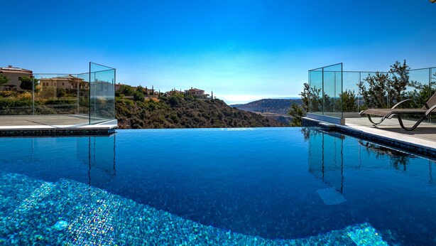 Uma piscina infinita azul cristalina com vista para uma encosta e montanhas ao longe.