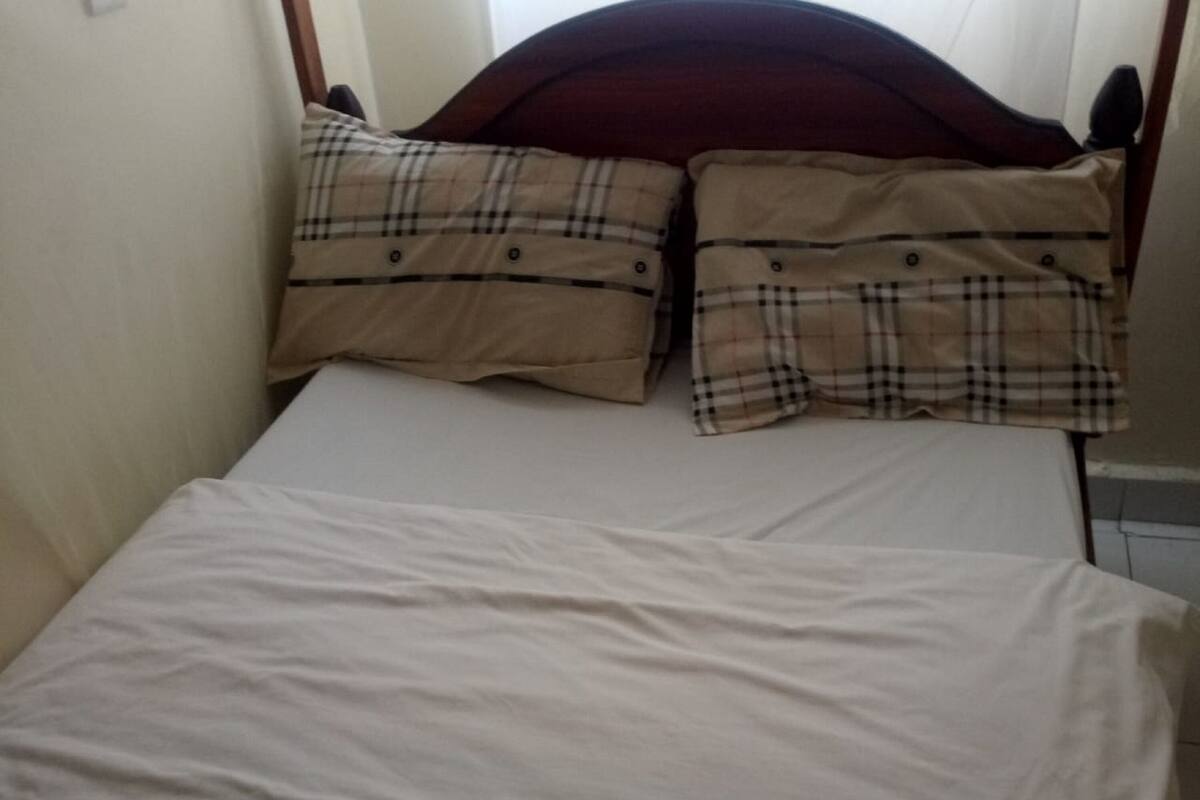 Uma cama com colchão branco e duas almofadas xadrez.