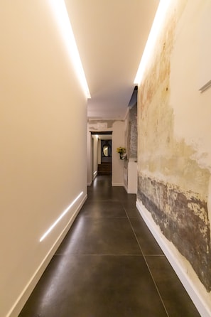 Um corredor com piso de azulejos escuros, paredes brancas e uma parede texturizada à direita.