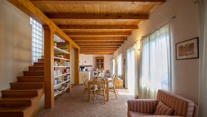 Uma sala de estar ampla com escada de madeira, mesa de jantar com cadeiras, sofá e estante de livros.