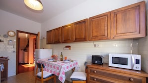 Cozinha com armários de madeira, micro-ondas, mesa com cadeiras e painel de azulejos.