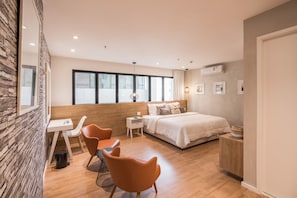 Quarto de hotel moderno com uma cama grande, uma escrivaninha com cadeiras, uma mesinha e uma lixeira.
