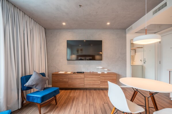 Uma sala de estar moderna com um armário de madeira, um sofá azul com almofada, uma mesa de jantar branca e um espelho grande na parede.
