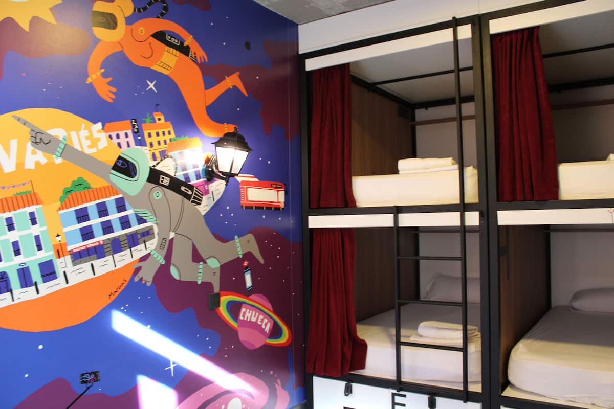 Quarto com beliches, um mural com arte temática espacial e uma cortina vermelha.