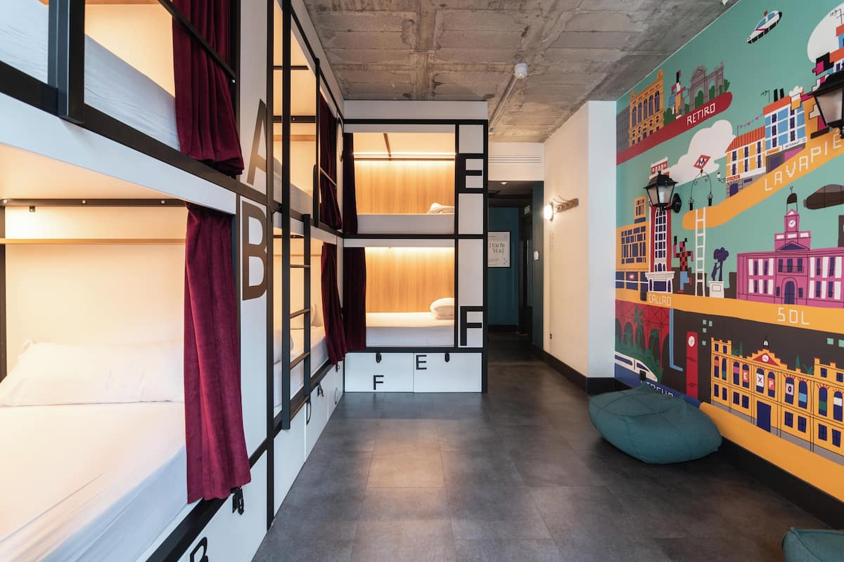 Quarto de hostel com beliches, um mural e uma poltrona saco.