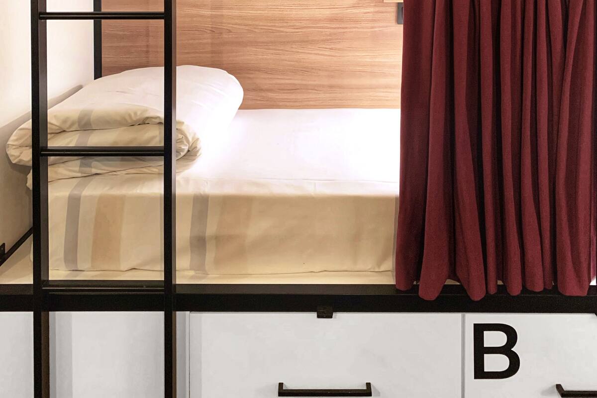 Uma cama box com beliche, cabeceira de madeira, colchão branco e cortina vermelha.