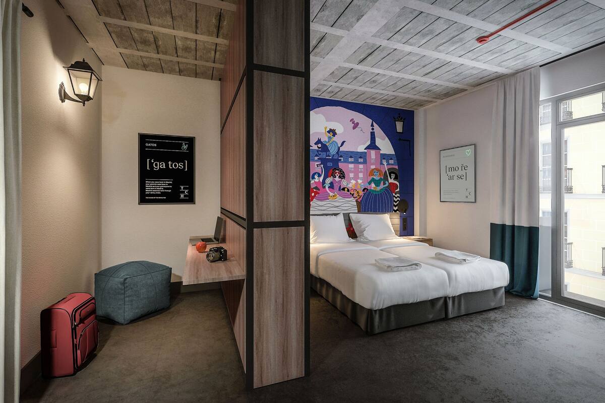 Quarto de hotel com cama, escrivaninha, cadeira e janela.
