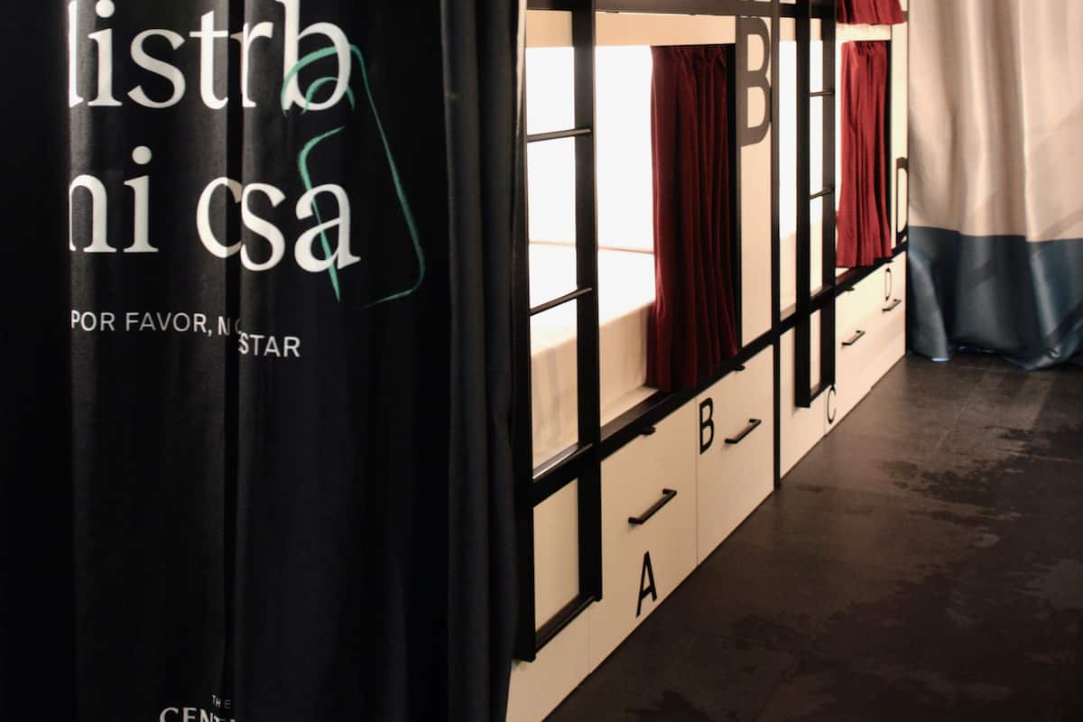 Quarto com beliches, cortinas pretas e teto de madeira.