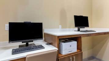 Um espaço de trabalho com dois monitores, um teclado, um rato e uma impressora sobre uma secretária branca, em frente a uma parede bege.