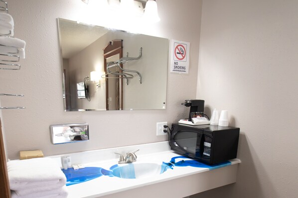 Casa de banho de hotel com lavatório, espelho, porta-toalhas e placa de 'Proibido Fumar'.