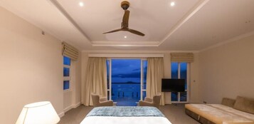 Quarto de hotel com cama, sofá, televisão e vista para o mar.