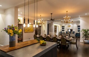 Cozinha moderna com luminárias pendentes, área de jantar com lustre e vista para a sala de estar.
