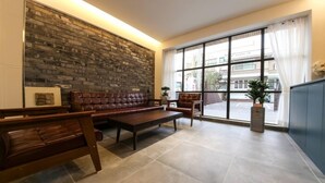 Uma sala de estar moderna com parede de pedra, sofás de couro, mesa de centro de madeira e grandes janelas com cortinas.