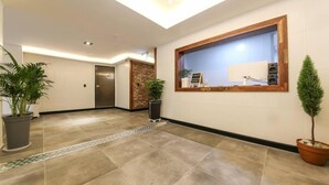 Um hall de hotel com piso de azulejos, um balcão de recepção com espelho e plantas em vasos.
