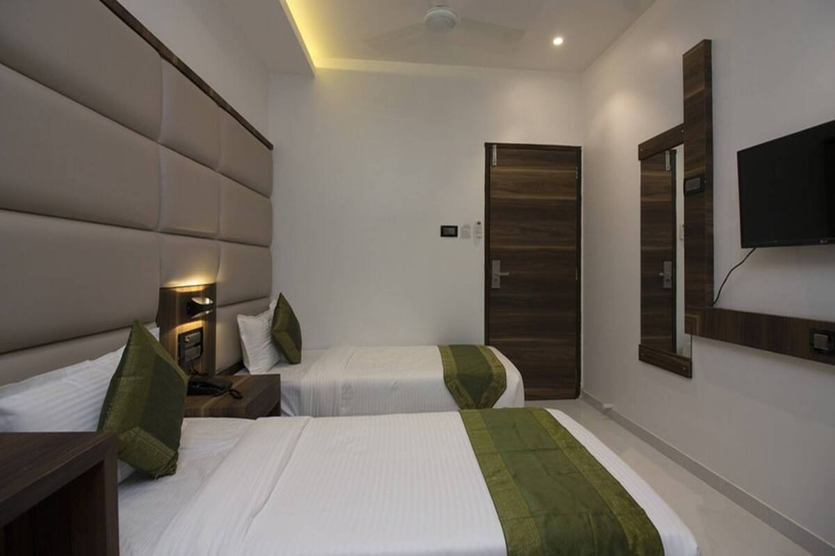 Quarto de hotel com duas camas, uma TV de tela plana na parede, um ventilador de teto e uma porta de madeira.