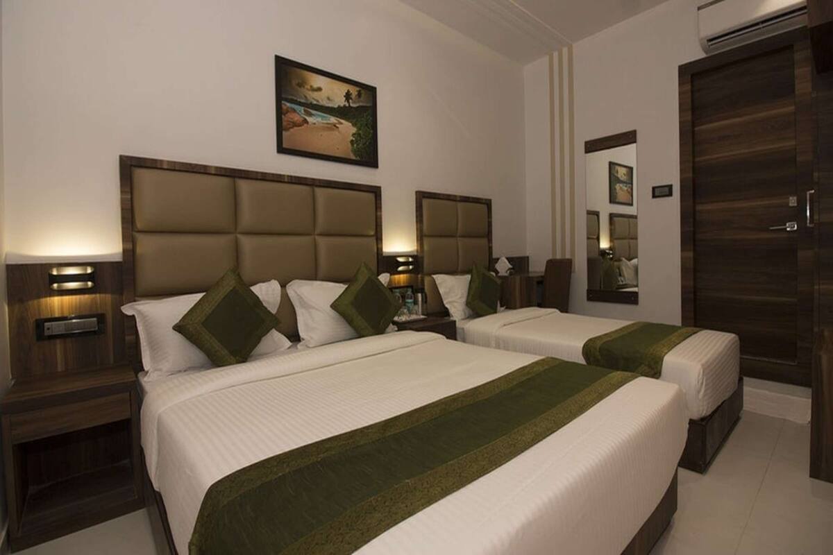 Quarto de hotel com duas camas, cada uma com cabeceira, mesas de cabeceira e abajures. Há um quadro na parede acima das camas e uma porta com um espelho.