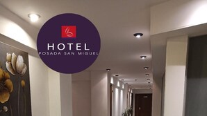Um corredor de hotel com uma área de recepção, um quadro de flores e uma planta em vaso.