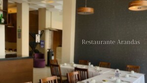 Restaurante com toalhas de mesa brancas, cadeiras de madeira e luminárias pendentes.