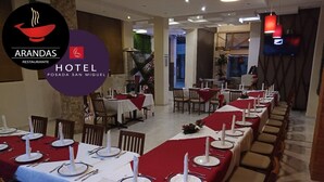 Uma sala de jantar de hotel com mesas preparadas para uma refeição, com toalha de mesa vermelha e pratos brancos.