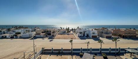 Uma área residencial à beira-mar, com vista desobstruída do oceano, uma praia de areia e uma área de piscina com guarda-sóis.