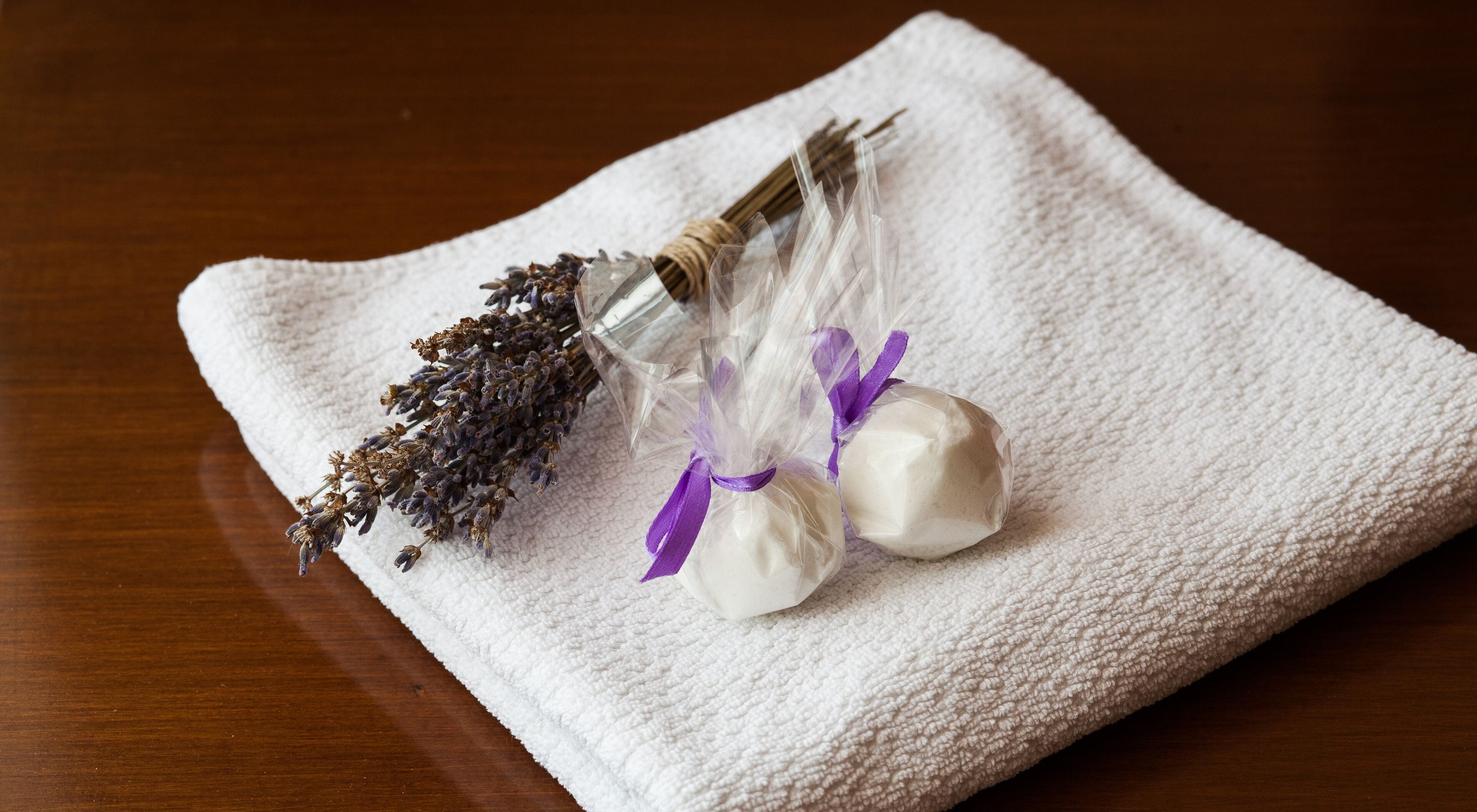Uma toalha branca com um raminho de lavanda seca e duas velas brancas amarradas com fitas roxas.