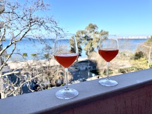 Duas taças de vinho numa varanda com vista para uma praia e o mar.