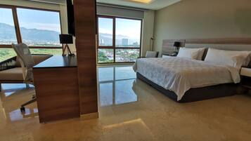 Quarto de hotel moderno com uma cama grande, uma escrivaninha e vista para o horizonte urbano através de amplas janelas.