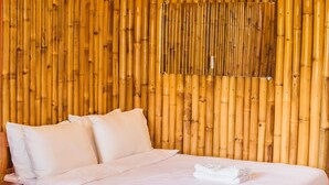 Quarto com duas camas, piso de madeira e parede de bambu.