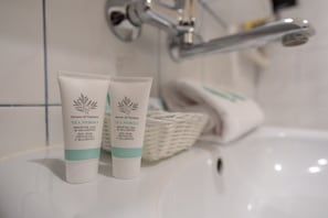 Duas garrafas de chá, gel de banho de neroli e shampoo em cima de uma pia de banheiro.