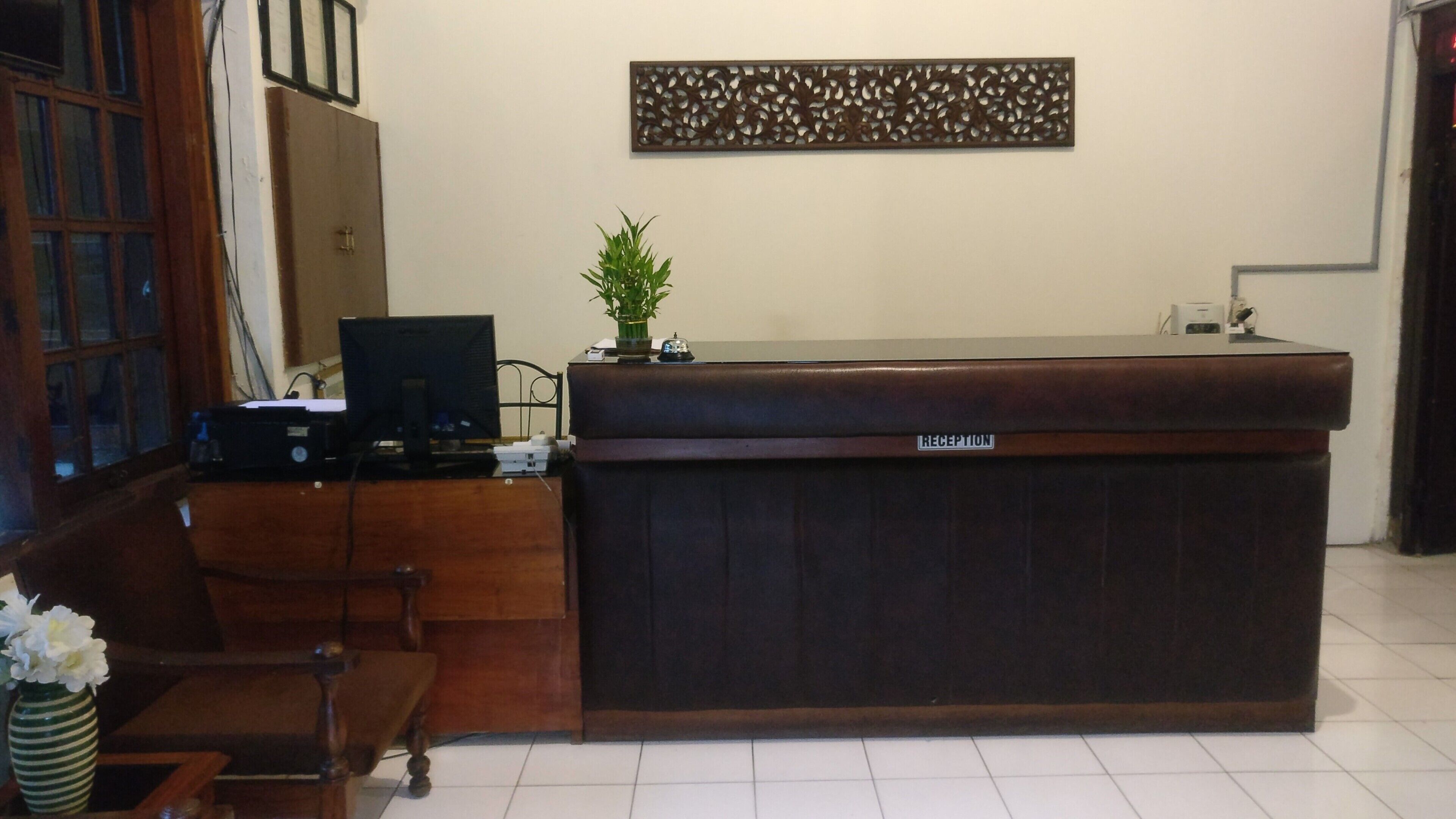 Balcão de recepção com computador, planta em vaso e um painel decorativo na parede.