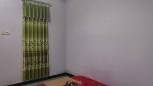 Quarto com uma cama de solteiro, janela com cortinas verdes e porta com barras verticais.