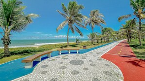 Caminho que leva a uma praia com palmeiras e céu azul e límpido.