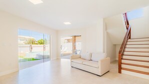 Ampla sala de estar com escada, sofá e porta de vidro que dá para uma área externa.