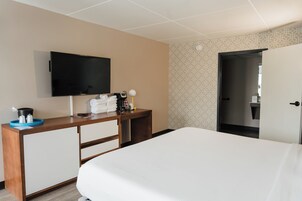 Quarto de hotel com cama, televisão na parede, escrivaninha com artigos de higiene e parede com padrão.