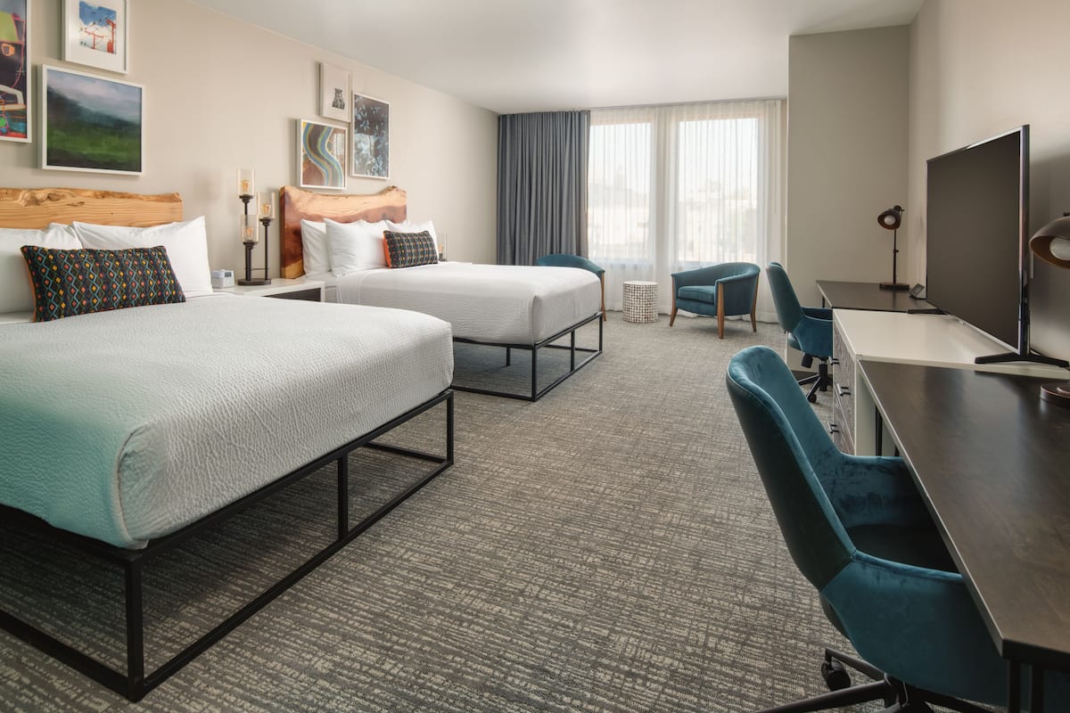 Quarto de hotel com duas camas, uma escrivaninha, uma cadeira e uma televisão.
