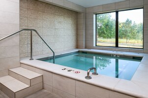 Uma piscina com degraus de acesso e uma janela com vista para árvores, com uma placa indicando a profundidade da piscina.
