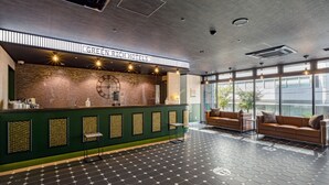 Um saguão de hotel com uma mesa de recepção, um relógio grande e uma área de estar com um sofá e poltronas.