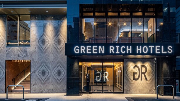 Exterior do Green Rich Hotels, com design moderno, destacando o logo 'DR' e uma entrada de vidro.