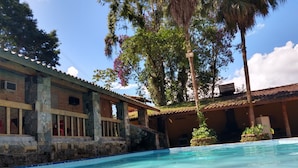 Uma área de piscina com um edifício de pedra, um alpendre coberto e árvores ao redor.
