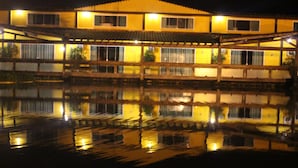 Um edifício de vários andares com fachada amarela e grandes janelas, refletindo na água em frente.